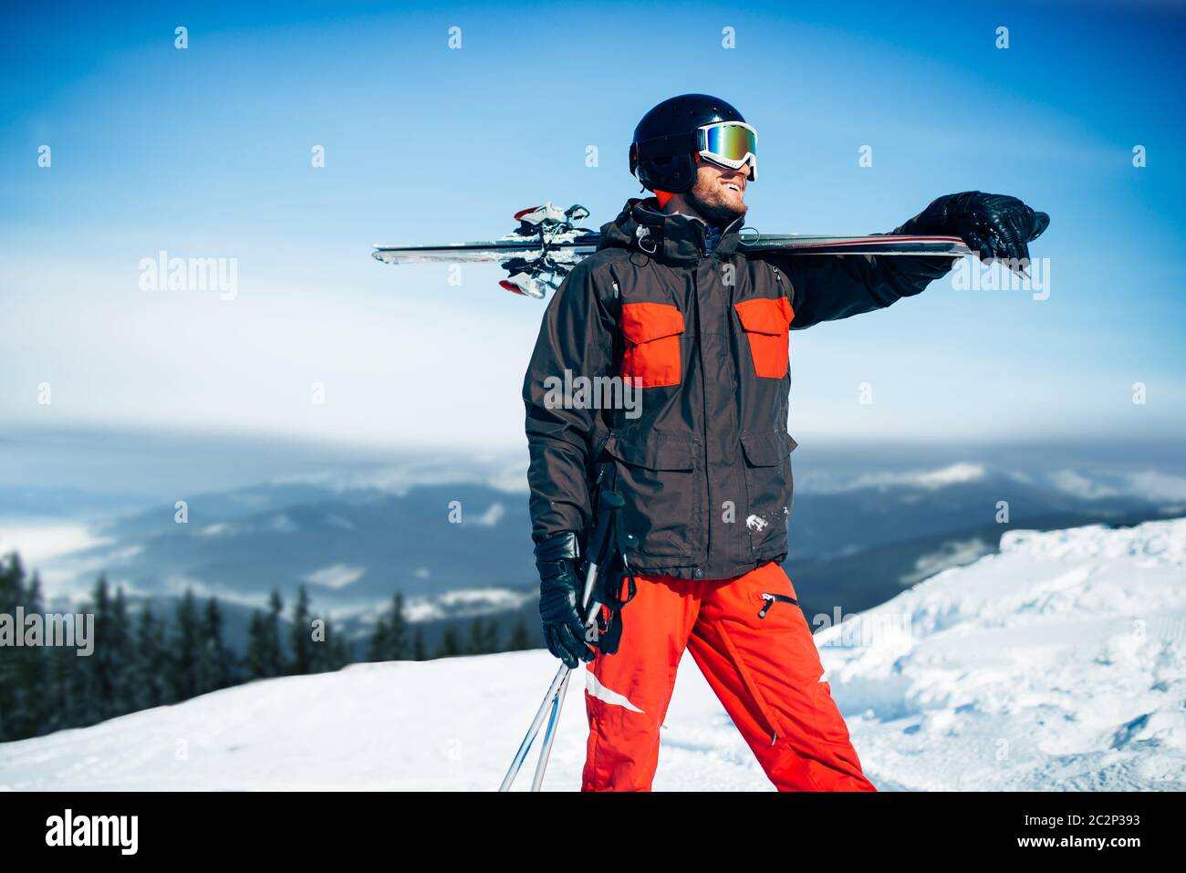 Skier poses with skis and poles in hands, blue sky and snowy mountains ...