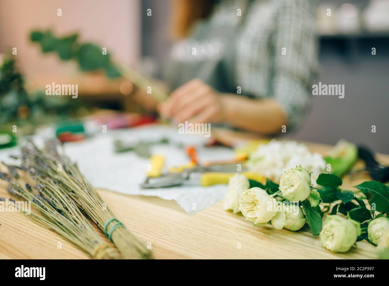 Female florist in apron prepares bouquet of white roses at workplace ...