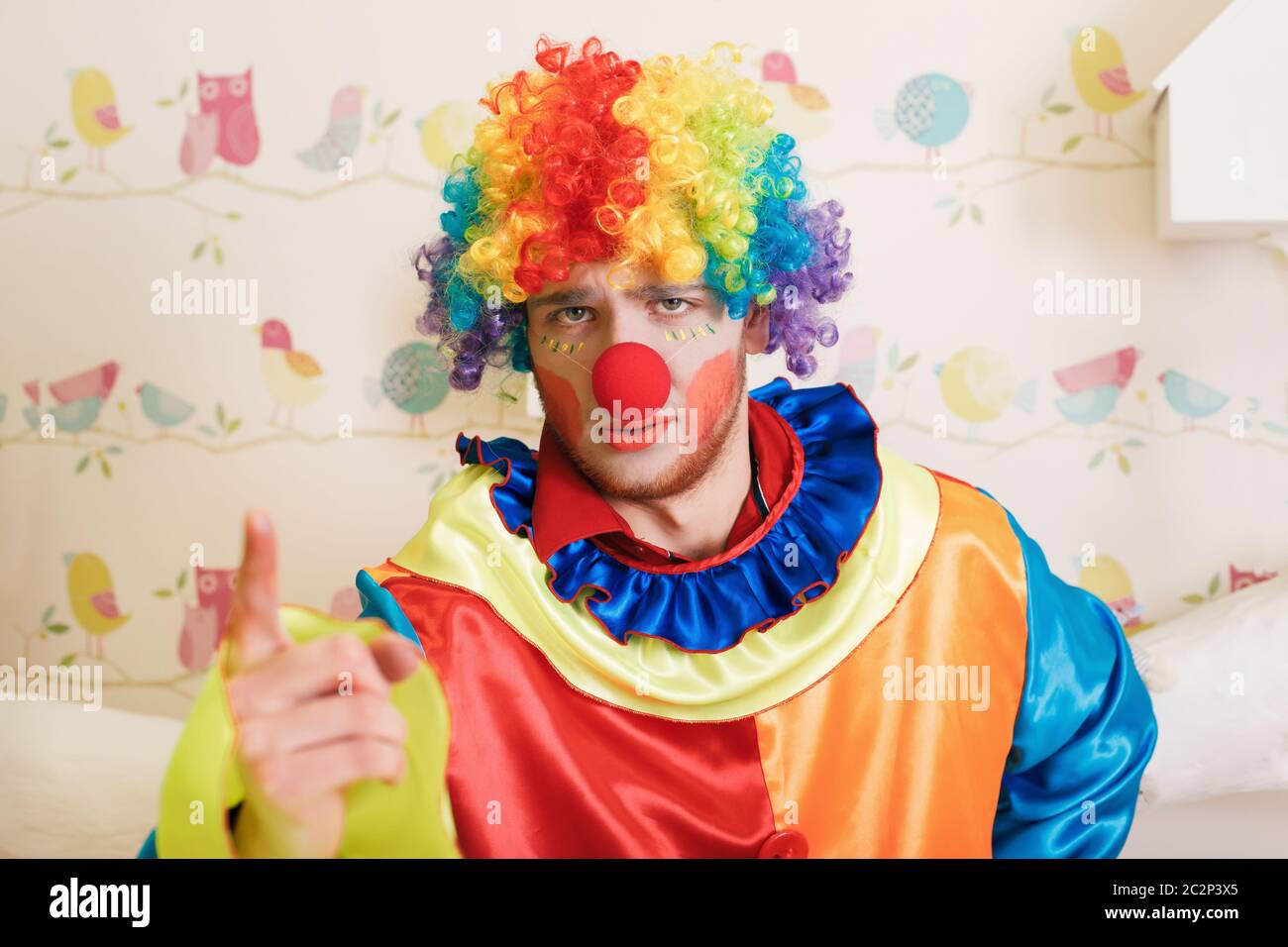 Clown in funny costume show finger. Decorative birds and nesting box on ...