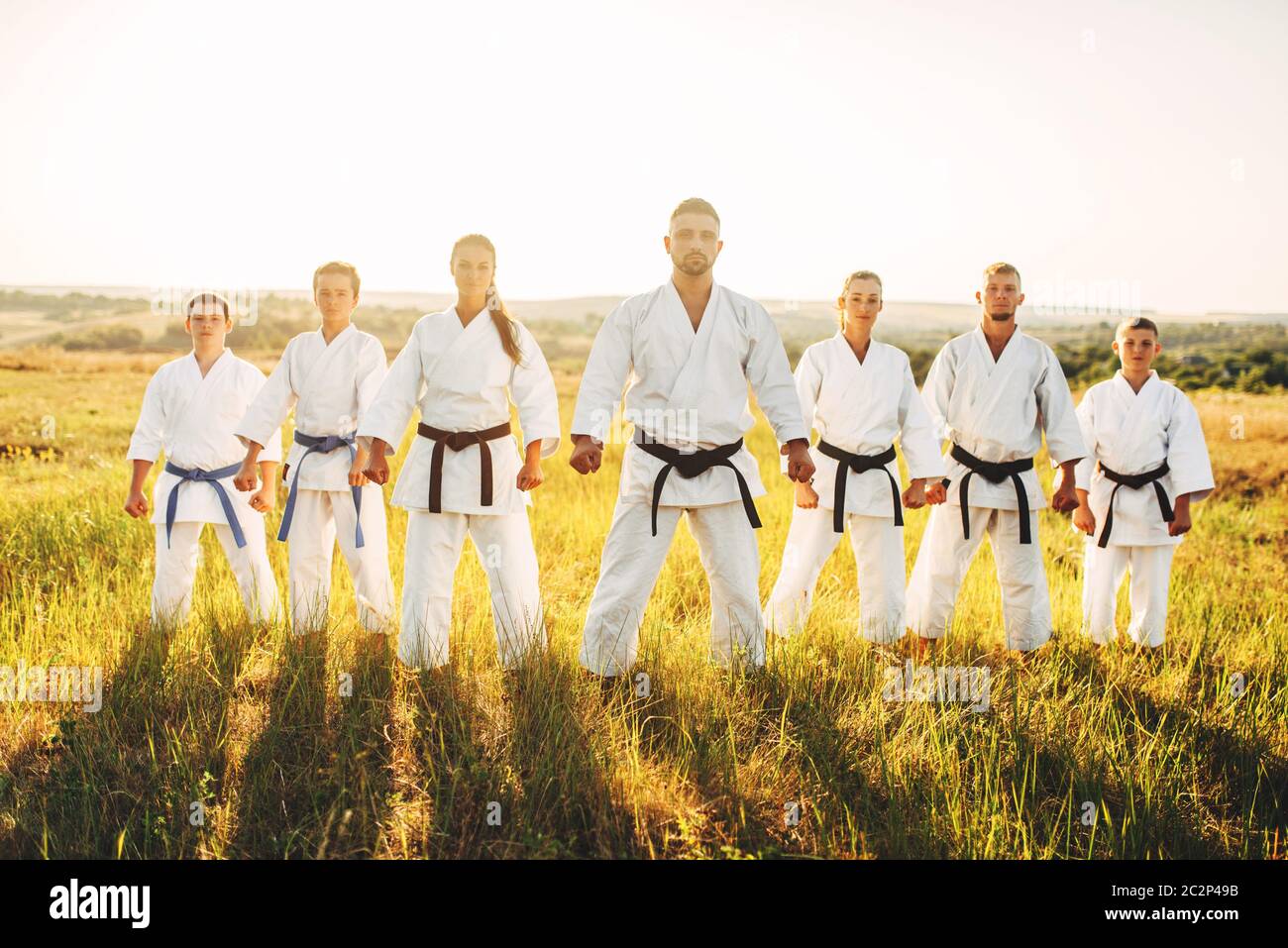 Karate group in white kimono, workout in summer field. Martial art training outdoor, black belt ...