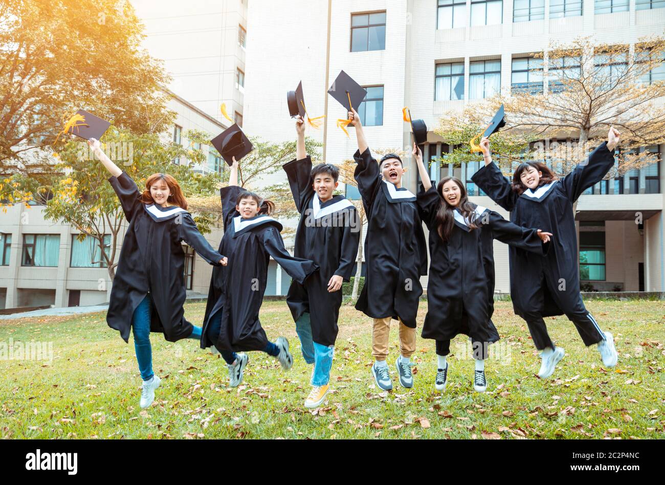 happy students in graduation gowns celebrating and jumping in ...
