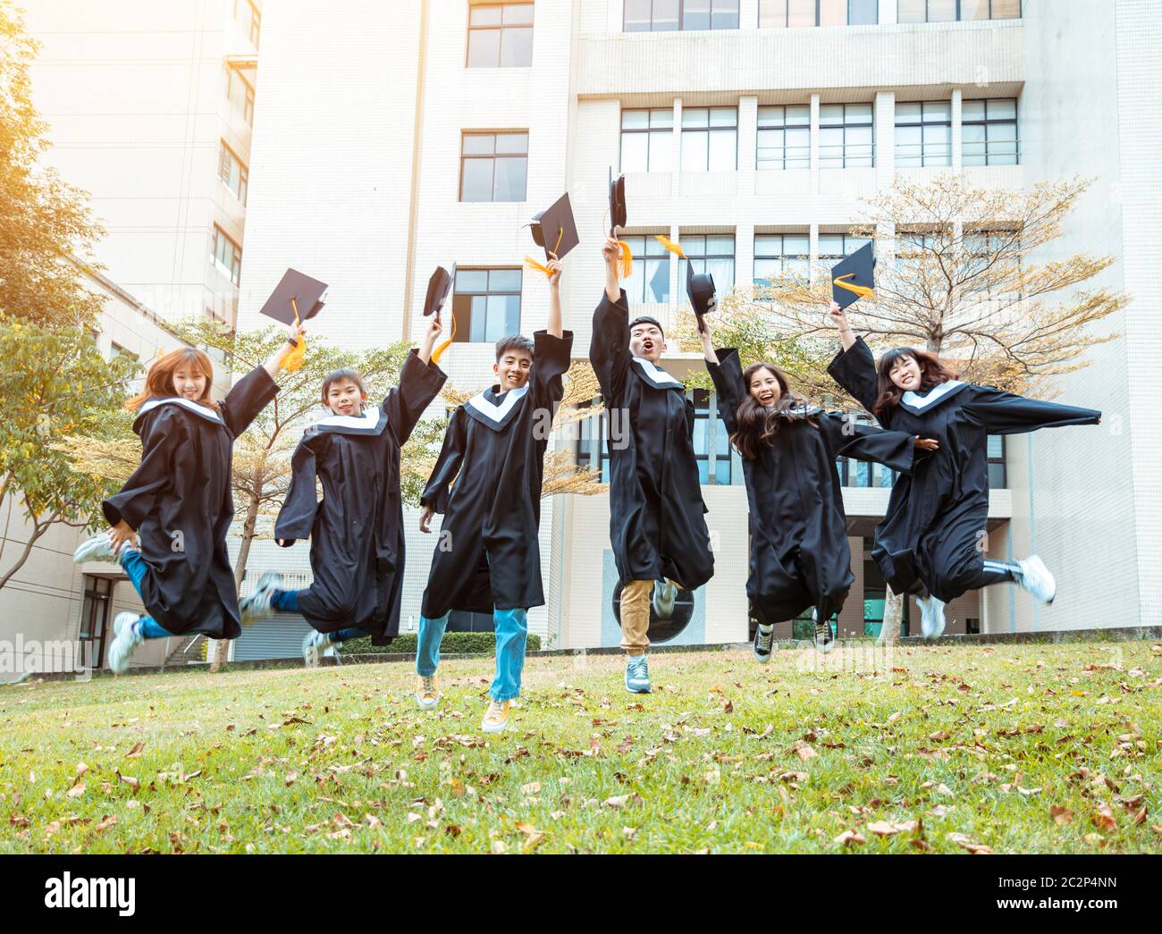 happy students in graduation gowns celebrating and jumping in ...