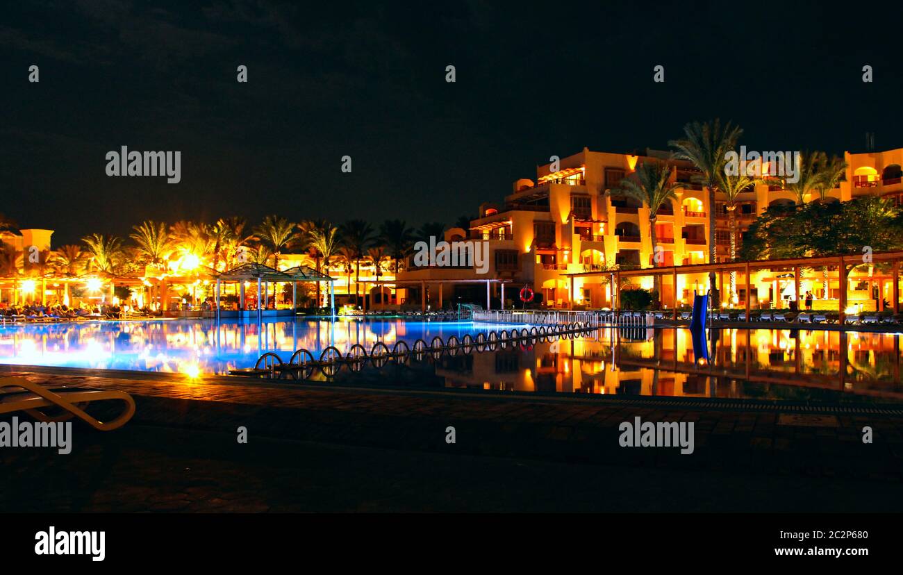 Lights of evening hotel are reflected in pool water in night. Bright ...