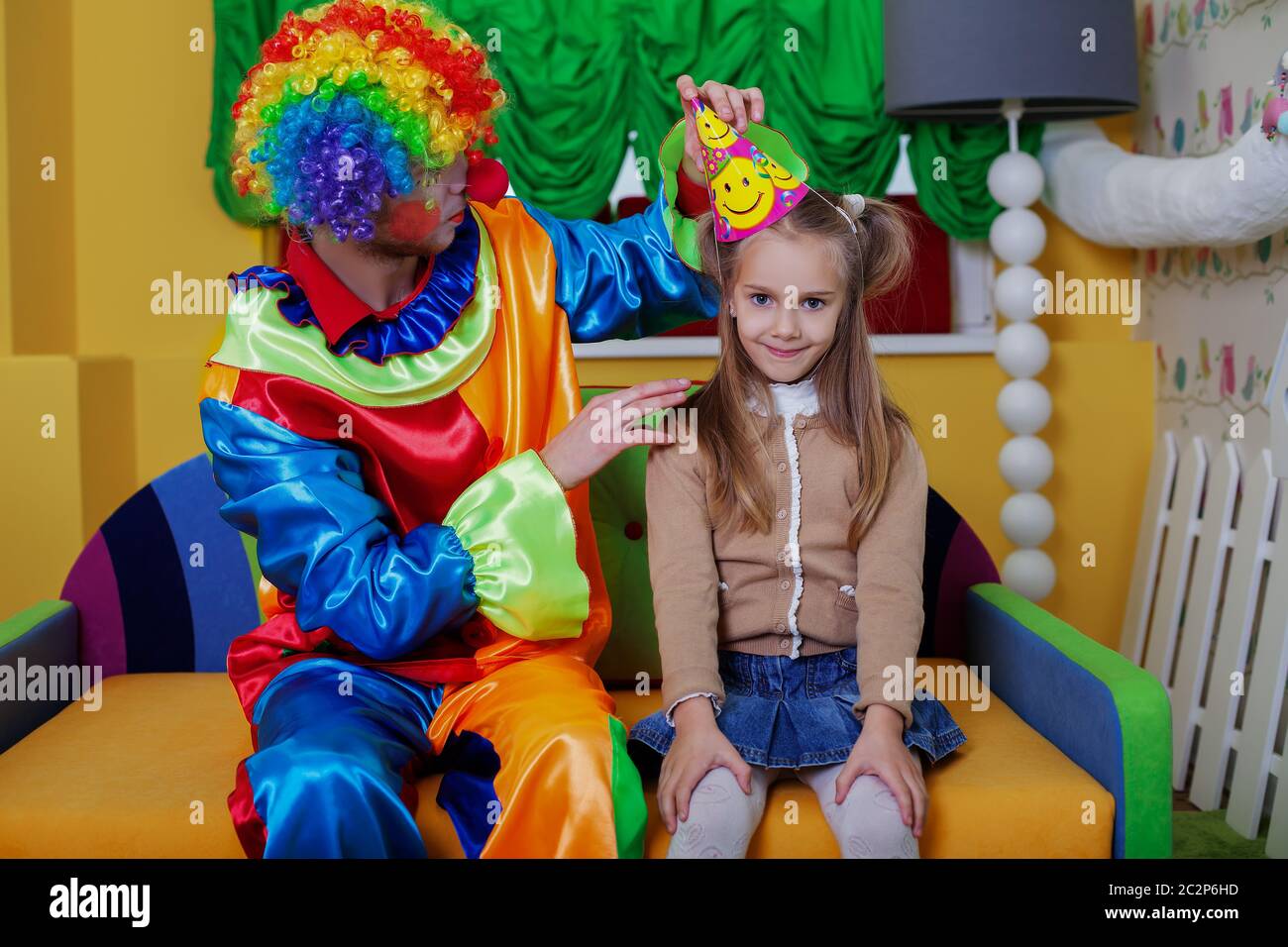 Little girl has put on a cap, and the clown laughs at her Stock Photo ...