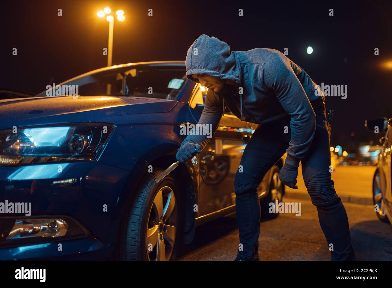 Car robber punctures the tyre, vandalism, hooligan. Hooded male bandit ...