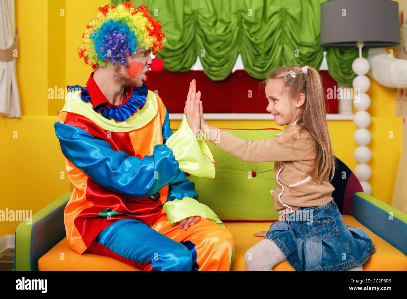 Happy little girl and clown play palms. Decorate studio on the ...