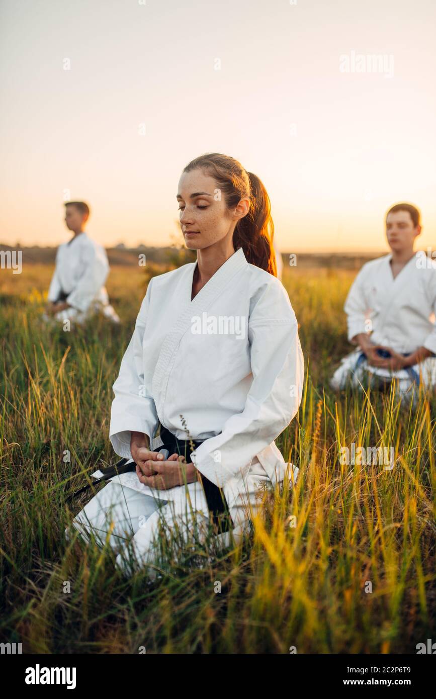 Karate class in white kimono meditates on training in summer field ...