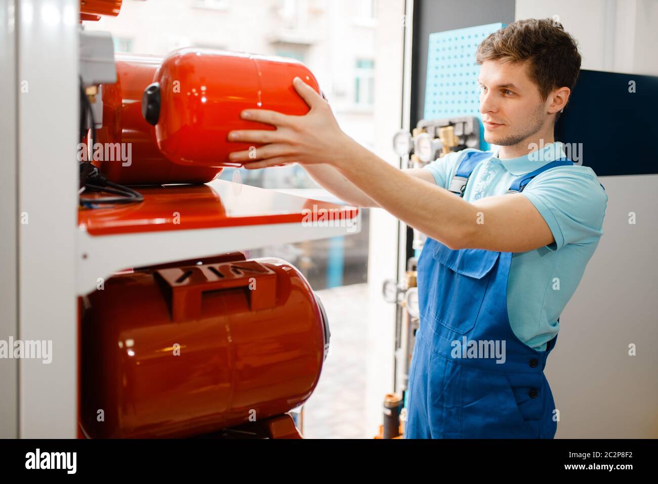 Plumber in uniform choosing expansion tank for water pump at showcase ...