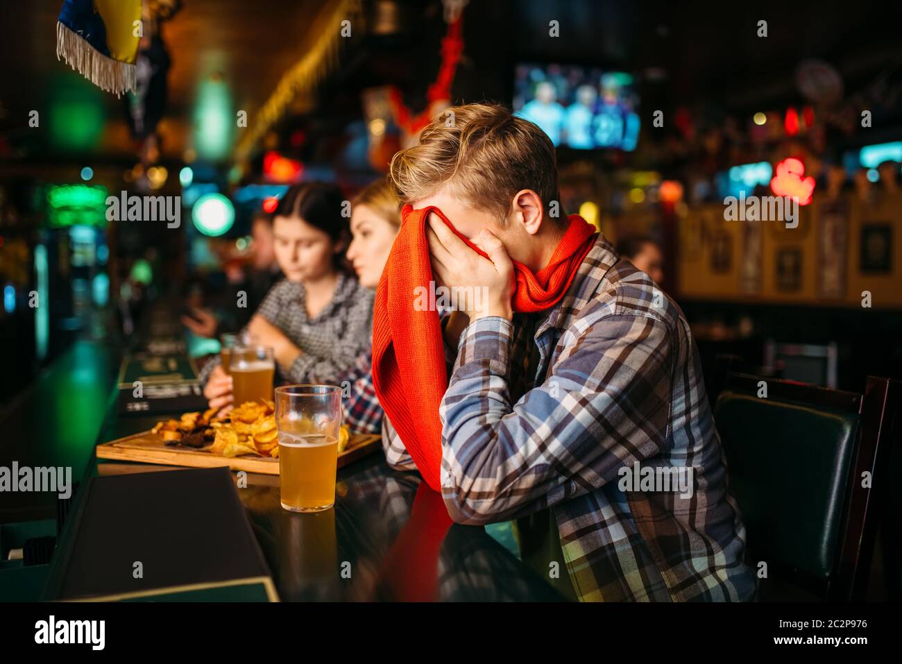 Sad football fan covers face with hands at the counter in sports bar ...