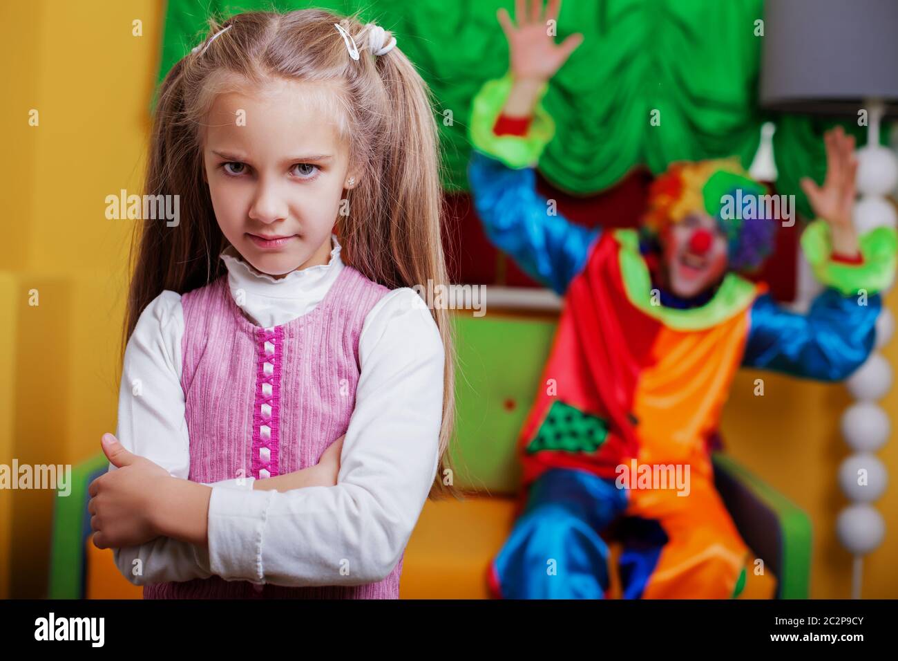 Upset little girl standing in the playroom. Funny clown on the ...