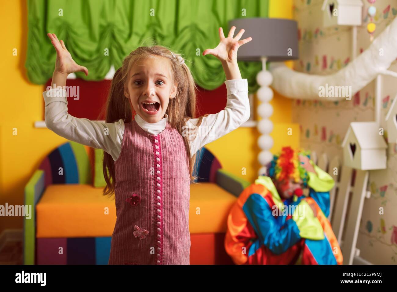 Little girl plays with upset clown at a birthday party. Colorful couch ...