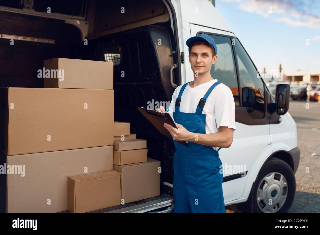 Deliveryman in uniform, carton boxes in the car, delivery service. Man ...