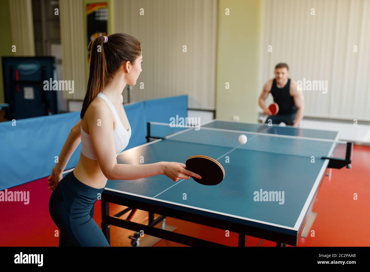 Man and woman playing ping pong indoors. Couple in sportswear holds ...