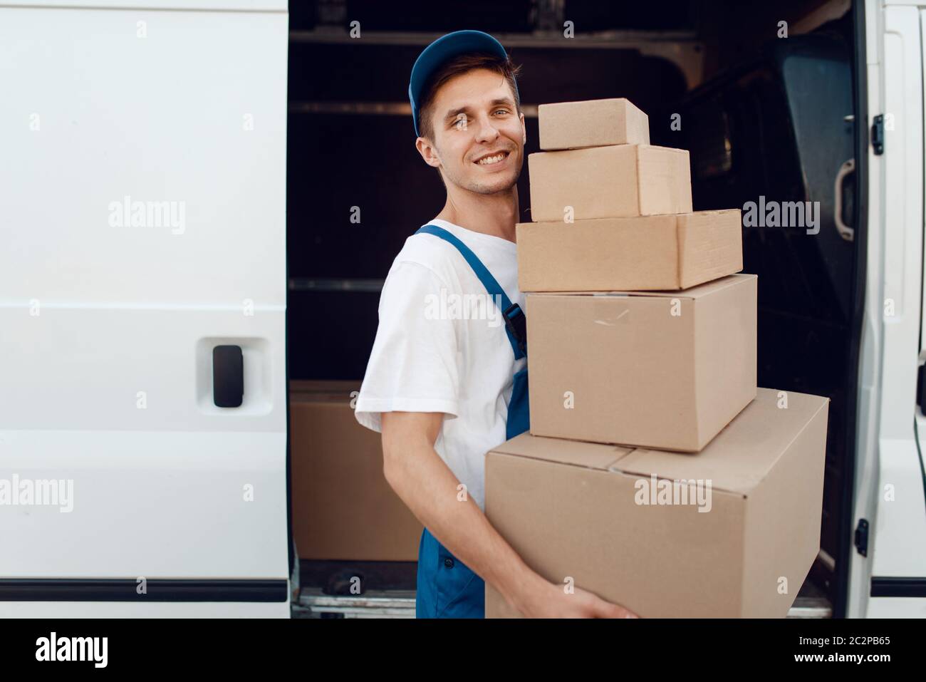 Mailman in uniform unloads the car with parcels, delivery service. Man ...