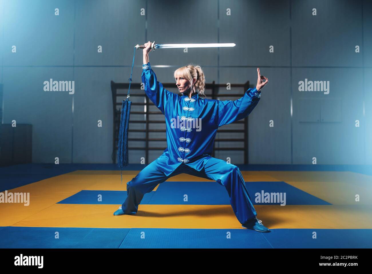 Female wushu fighter with sword in action, martial arts. Woman in blue ...