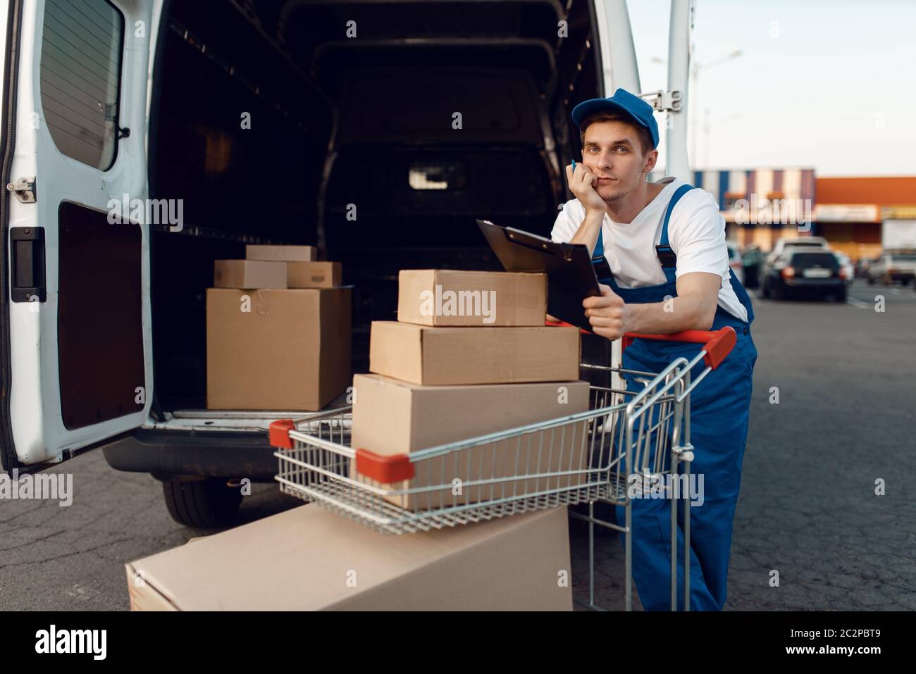Deliveryman in uniform holds cart with boxes at the car with parcels ...