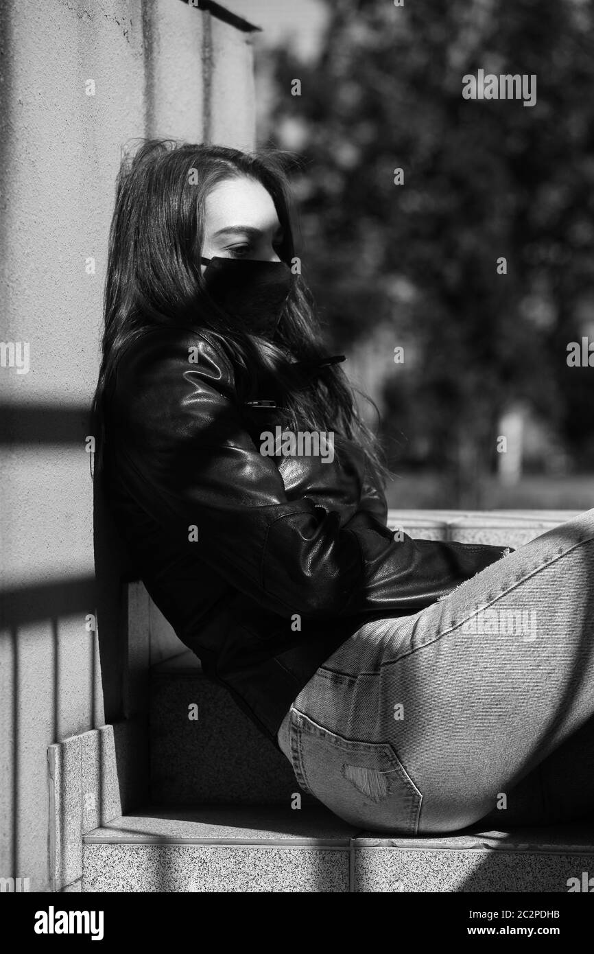 single sad young woman in medical protective mask sitting on steps ...