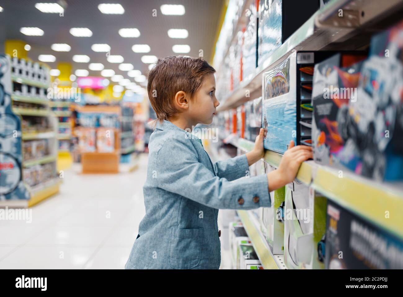 Little boy at the shelf in kids store, side view. Son choosing toys in ...