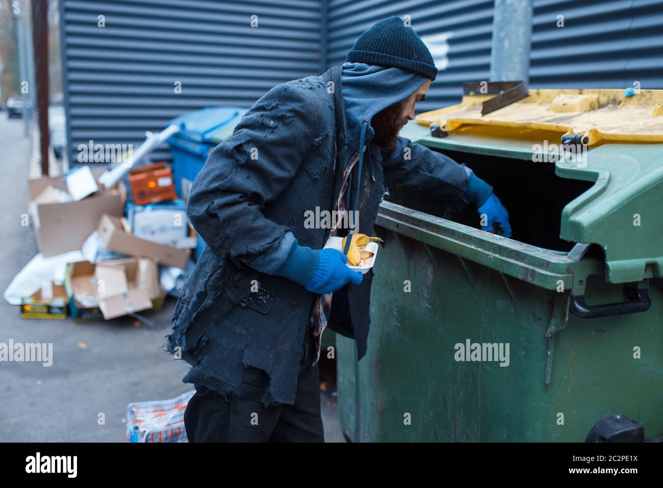 Male bearded beggar searching food in trashcan on city street. Poverty ...