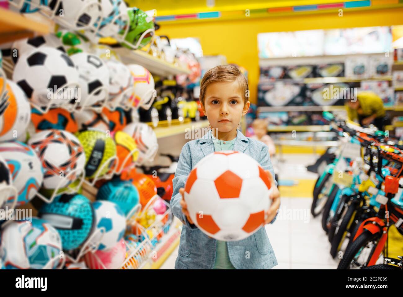 Little boy with ball in kids store, front view. Son choosing toys in ...