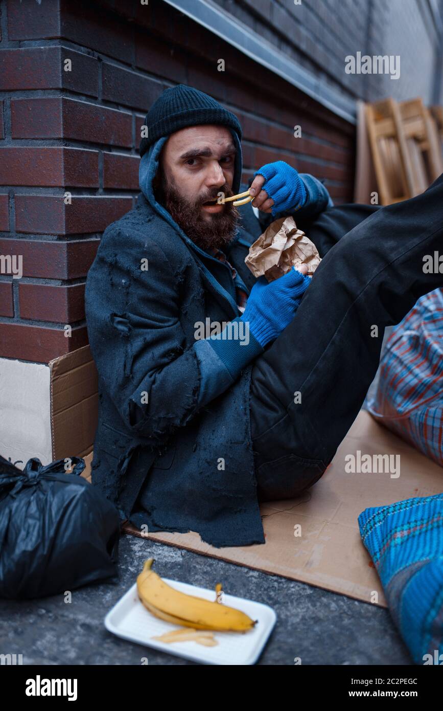 Bearded beggar eats burger on city street. Poverty is a social problem ...