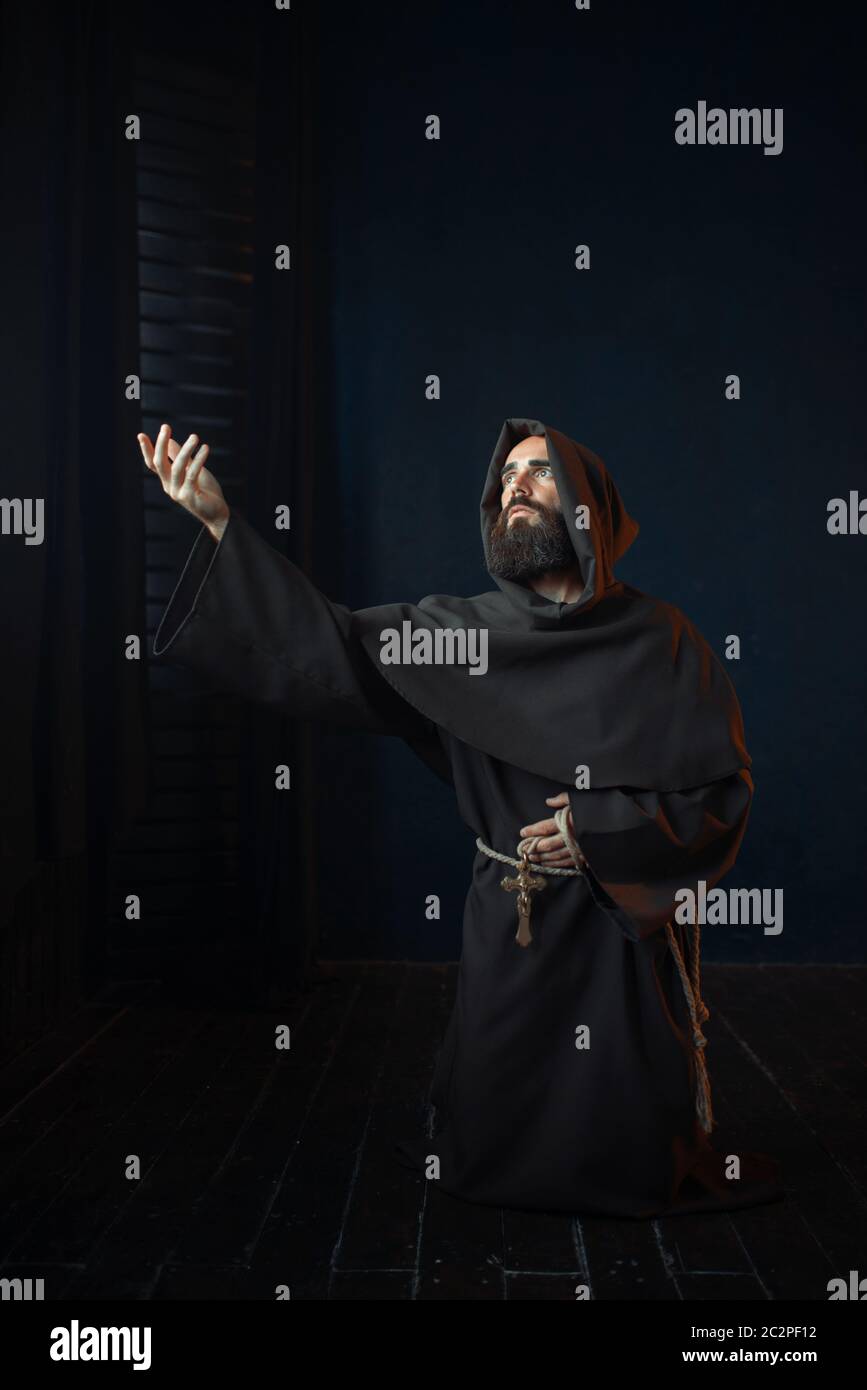 Medieval monk kneeling and praying, religion. Mysterious friar in dark ...