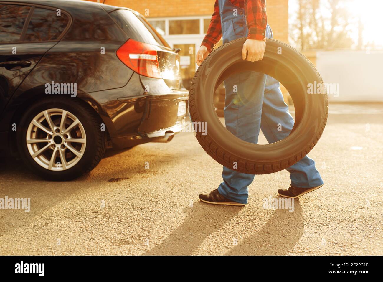 Male worker in uniform holds tyre, tire service. Vehicle repair service ...
