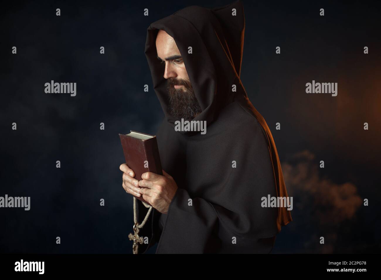 Medieval monk praying with book and cross in hands in church, secret ...