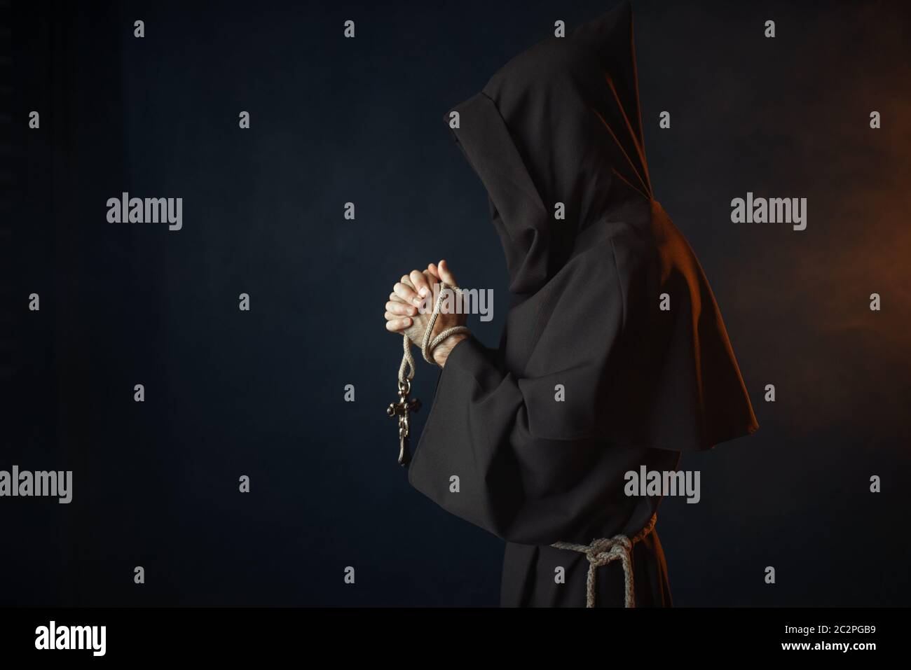 Medieval monk in black robe with hood praying with closed eyes, secret ...