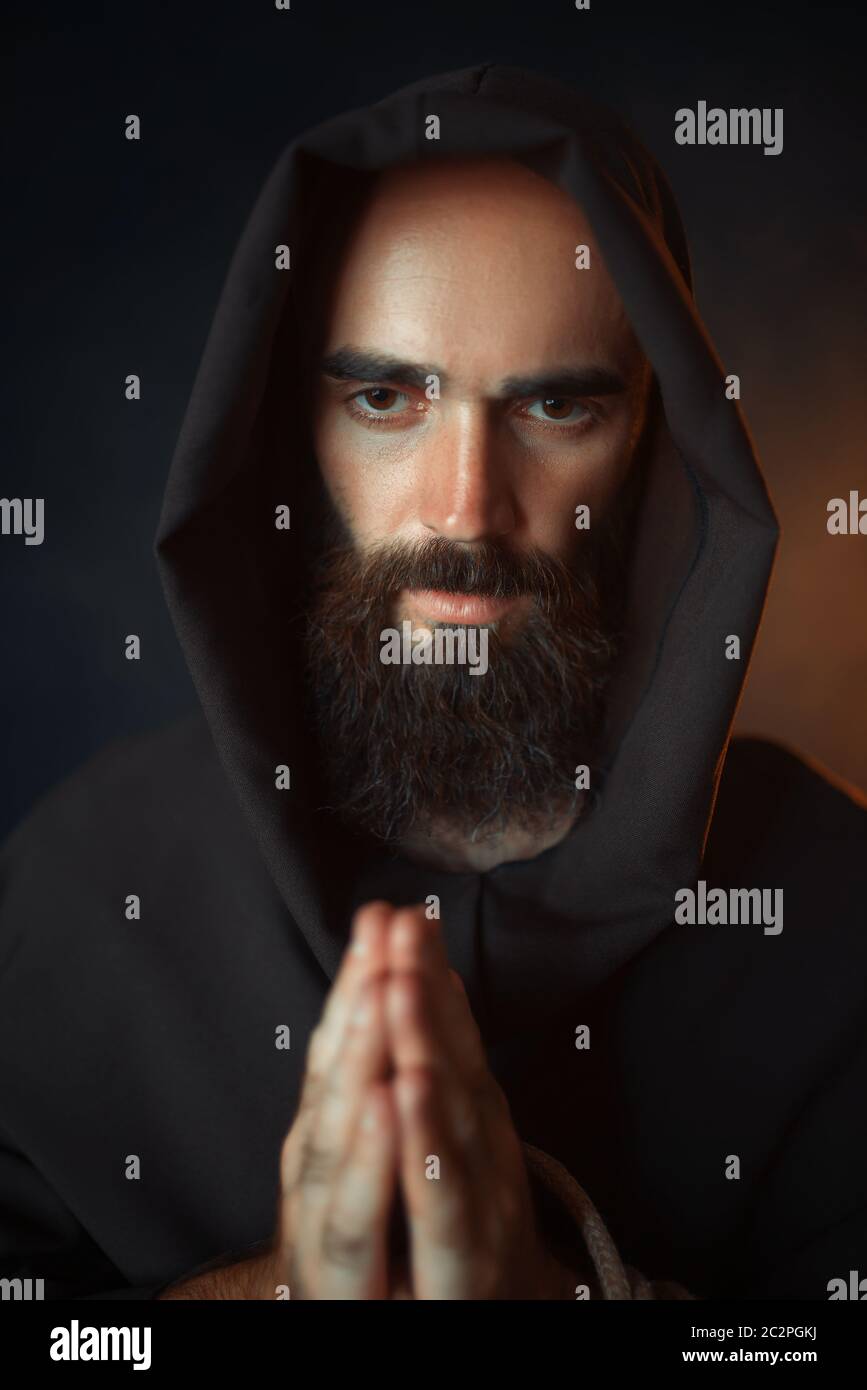 Medieval monk in black robe with hood praying with closed eyes, secret ...