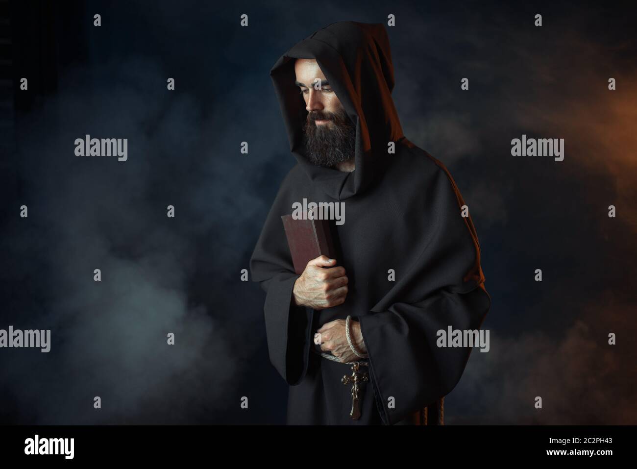 Medieval monk in robe holds spellbook in hands, black background ...