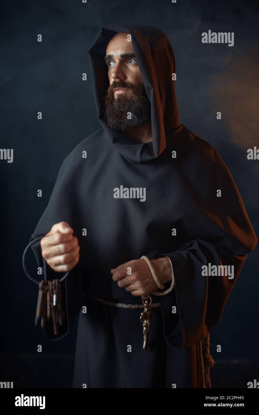 Medieval monk in robe holds a bunch of keys in hands, black background ...