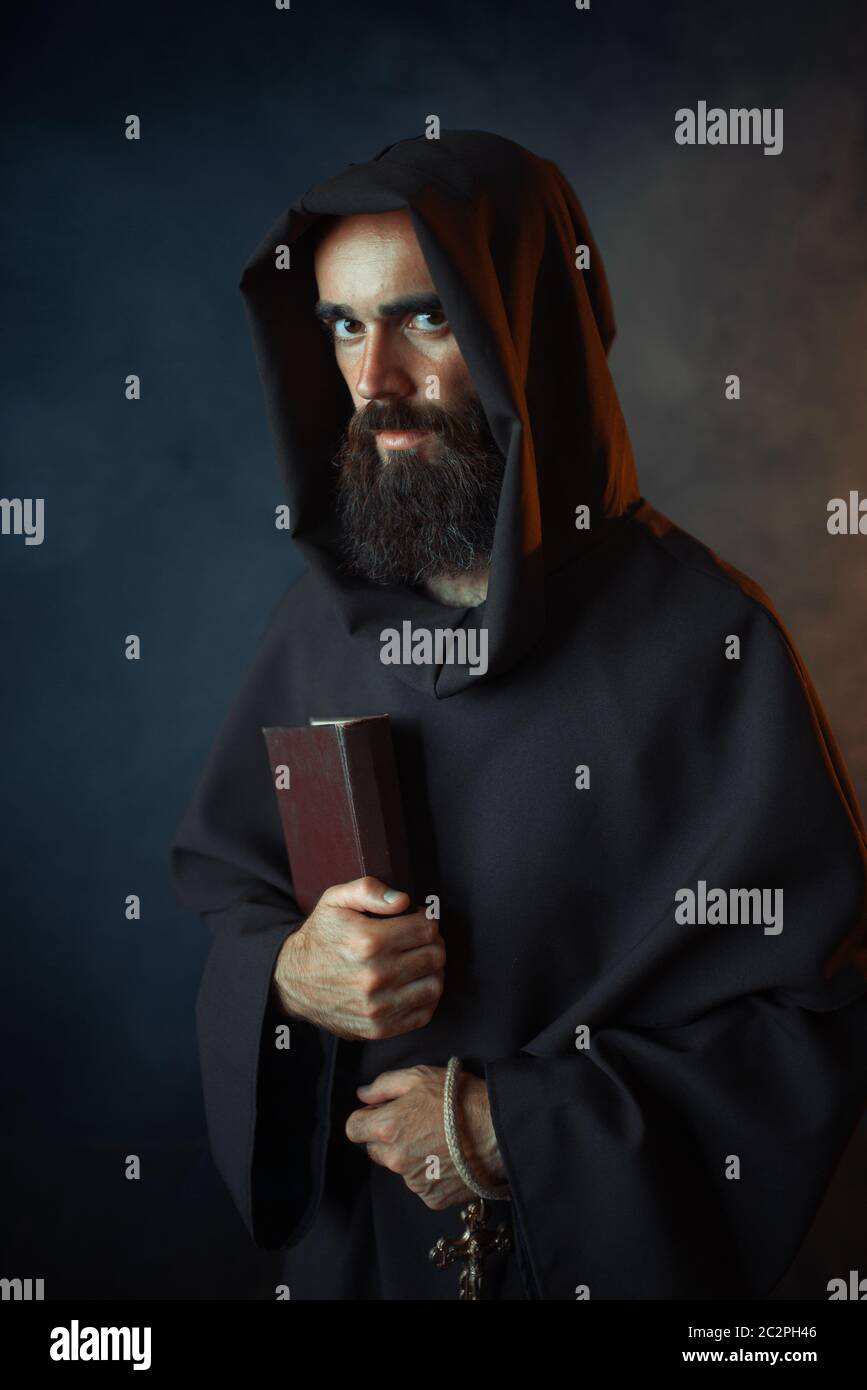 Medieval monk in robe holds spellbook in hands, black background ...