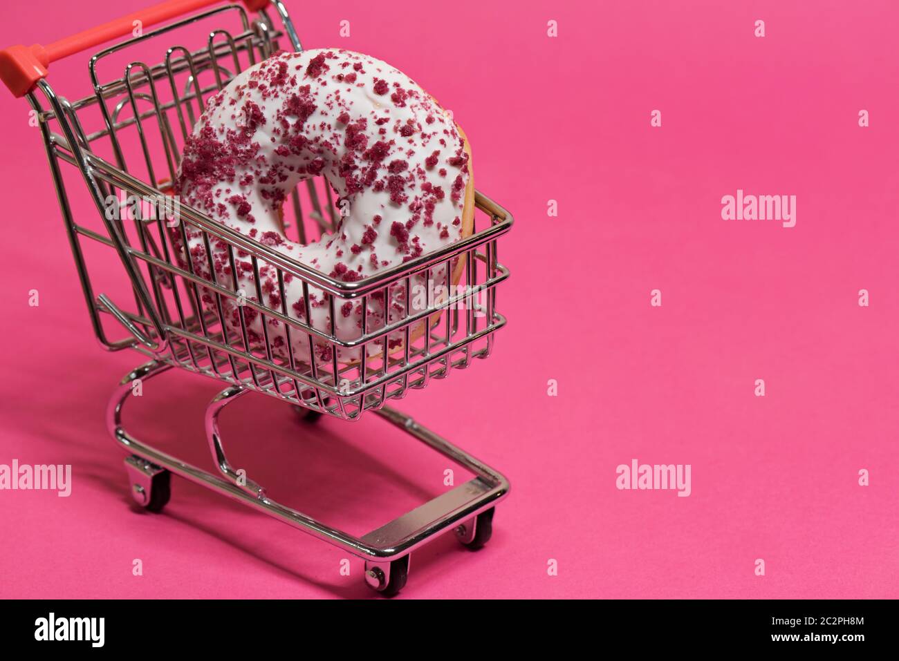 Macro shoot of white donut in shopping trolley over pink background ...