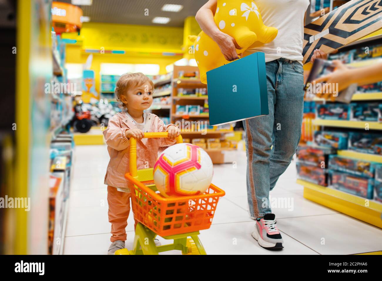 Mother with her little girl buying a lot of toys in kids store. Mom and ...