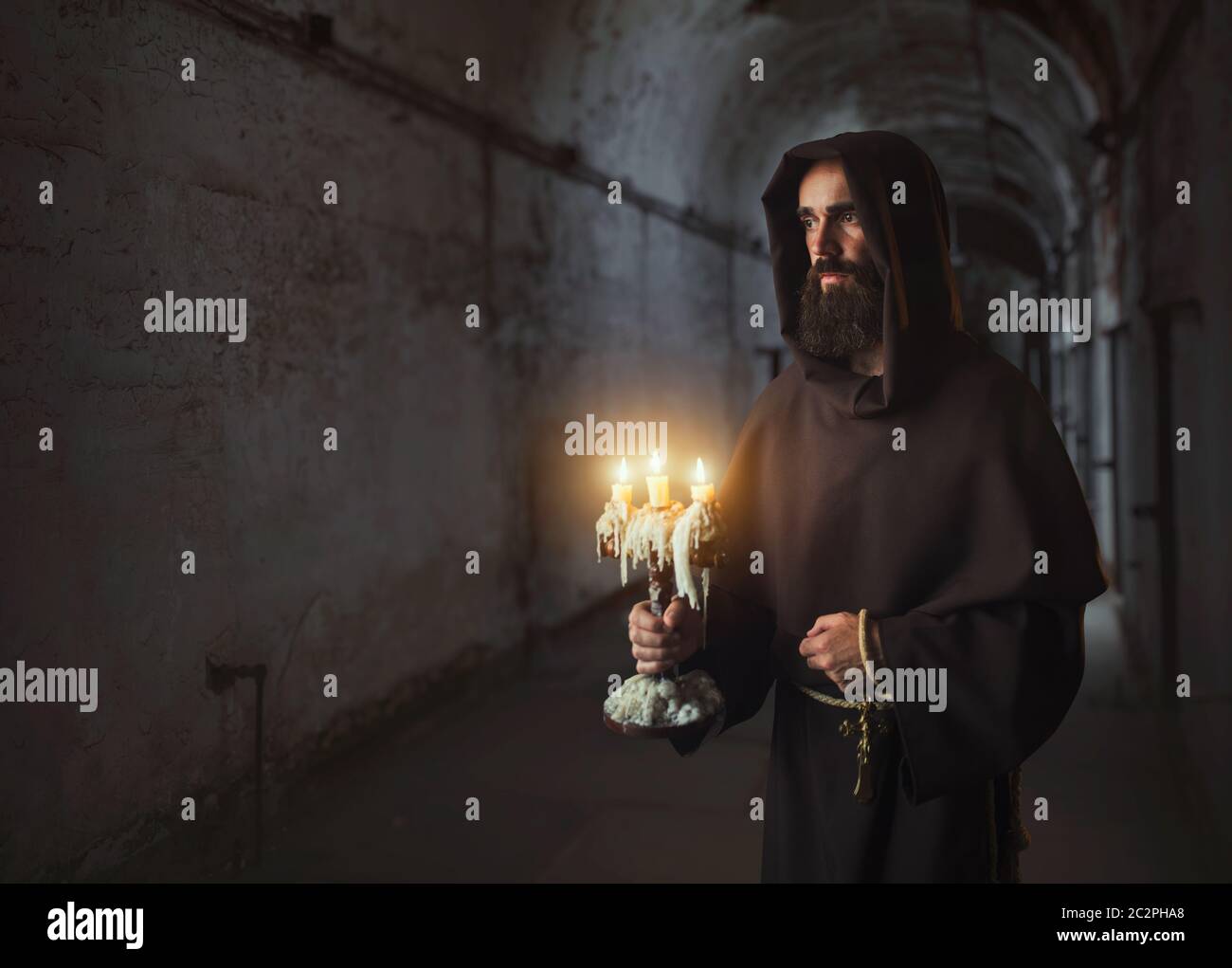 Medieval monk in robe holds a candlestick in hands in the temple ...