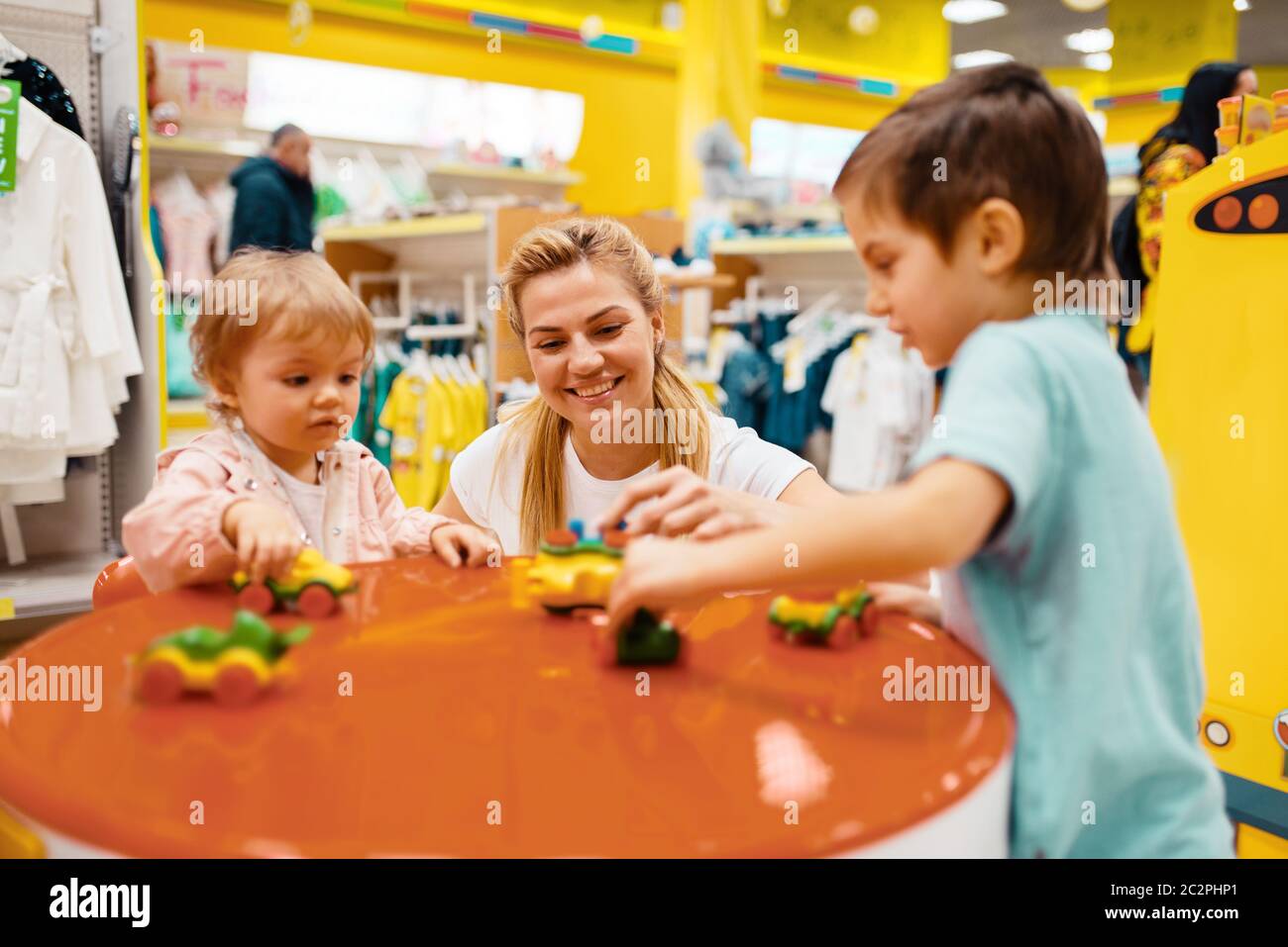 Mother with her little children playing in kids store. Happy mom with ...