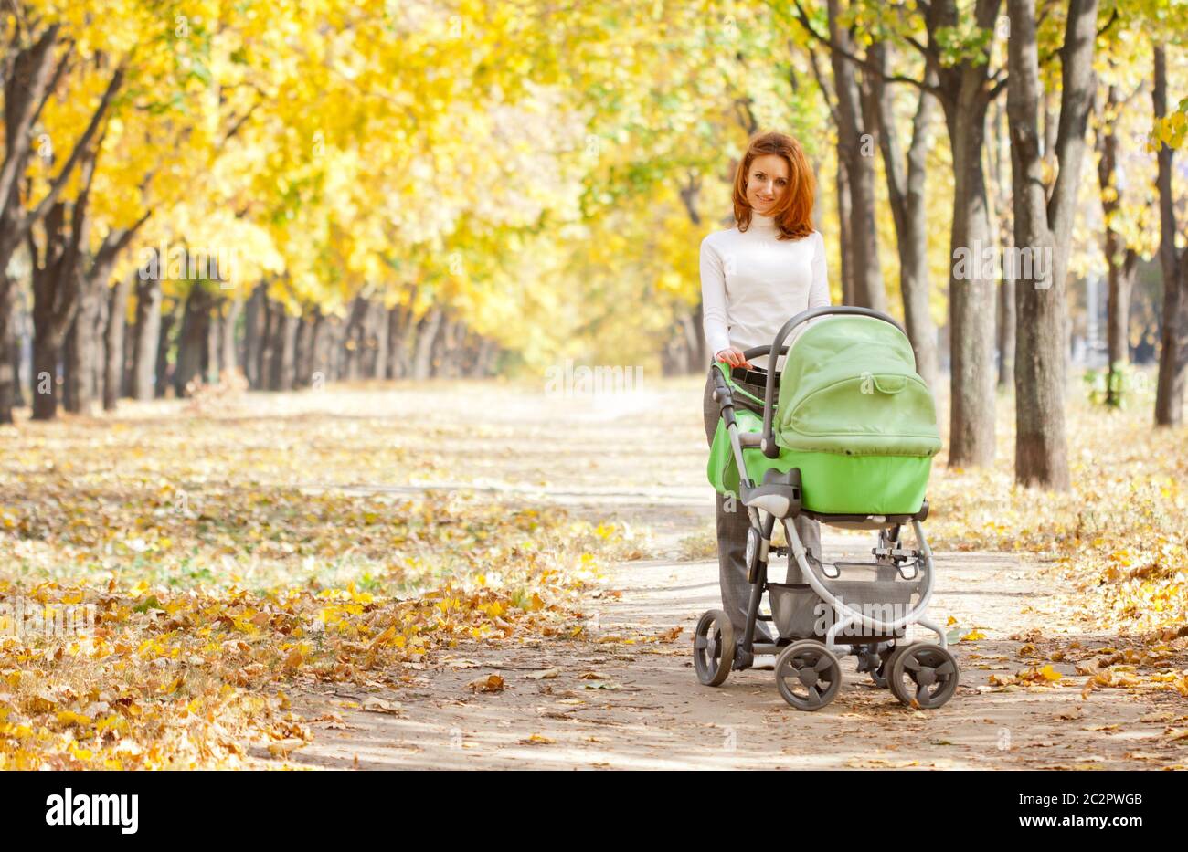 Happy young mother with baby in buggy walking in autumn park Stock ...