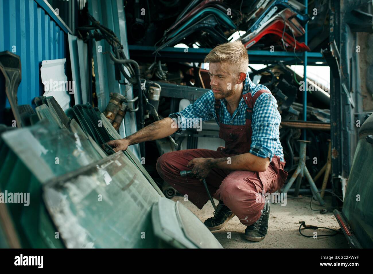 Dirty male repairman choosing glass on car junkyard. Auto scrap ...