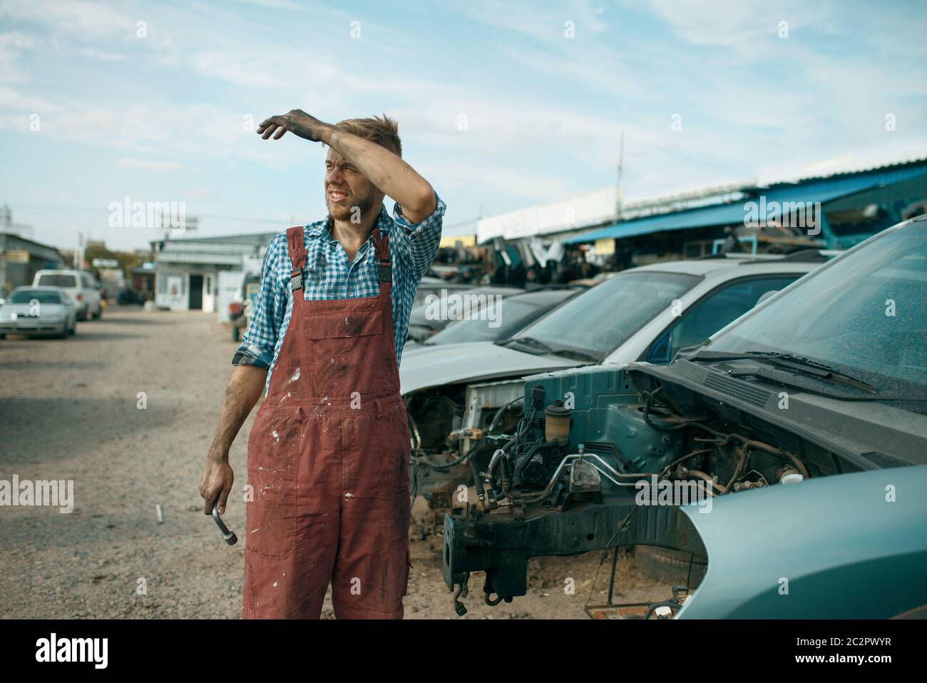 Tired male repairman with wrench on car junkyard. Auto scrap, vehicle ...