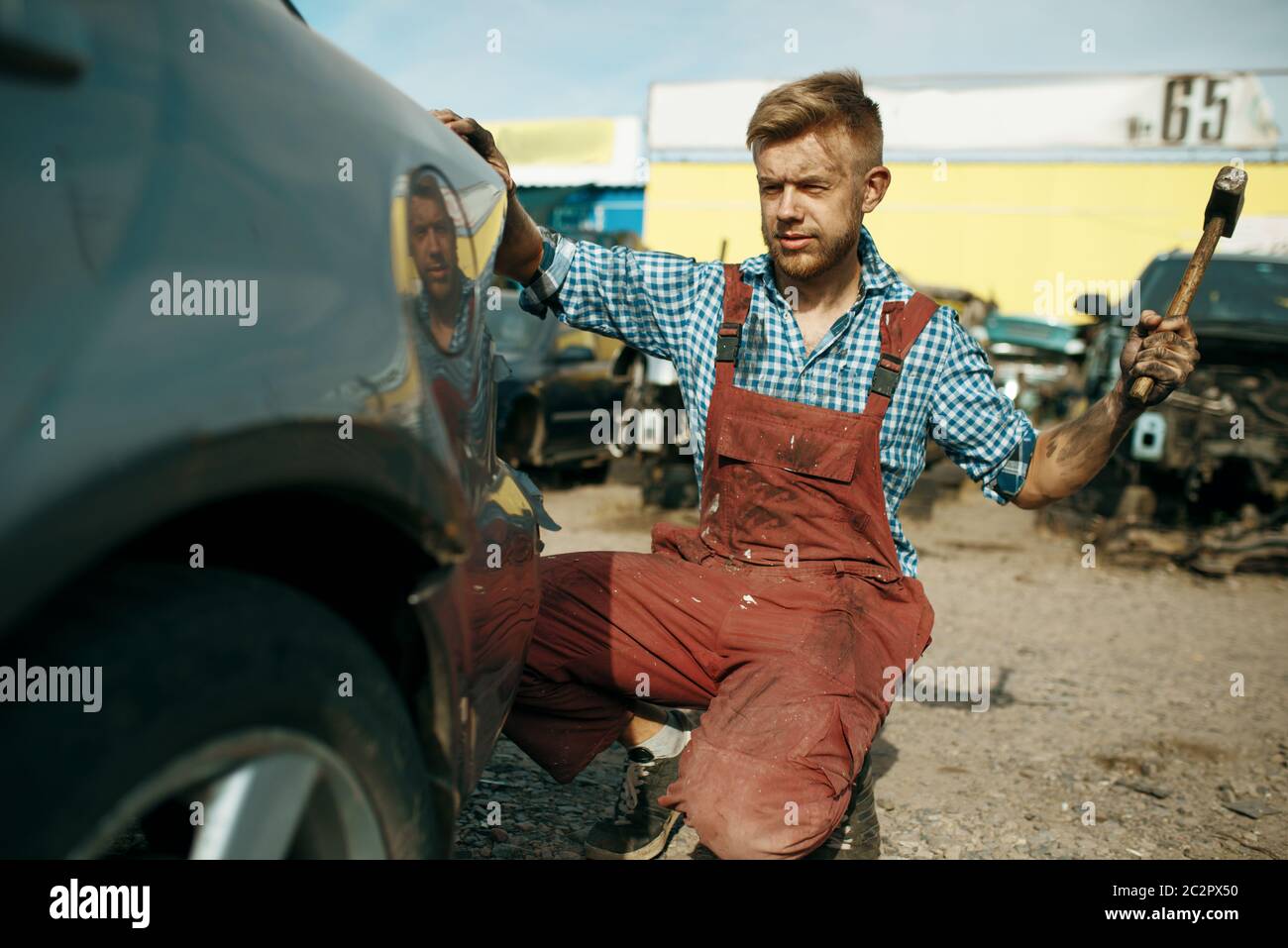 Male repairman works with hammer on car junkyard. Auto scrap, vehicle ...