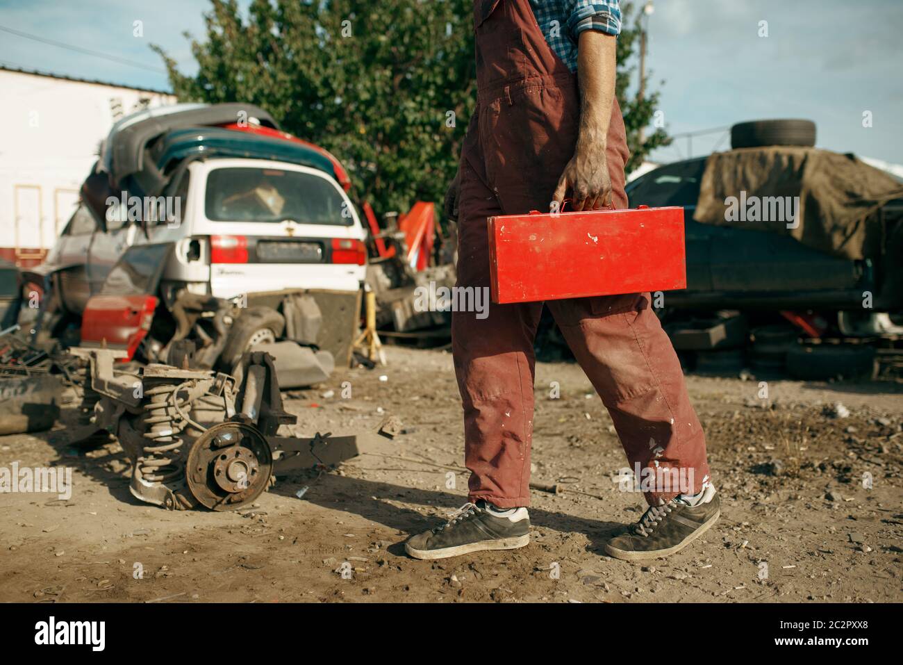 Male repairman holds toolbox on car scrapyard. Auto scrap, vehicle junk ...