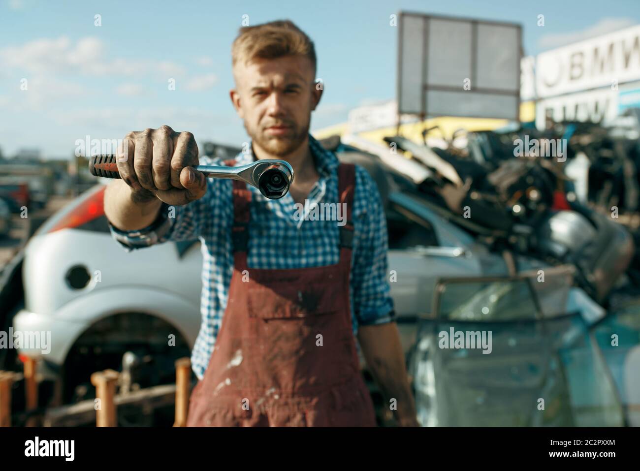 Male repairman shows wrench on car scrapyard. Auto scrap, vehicle junk ...