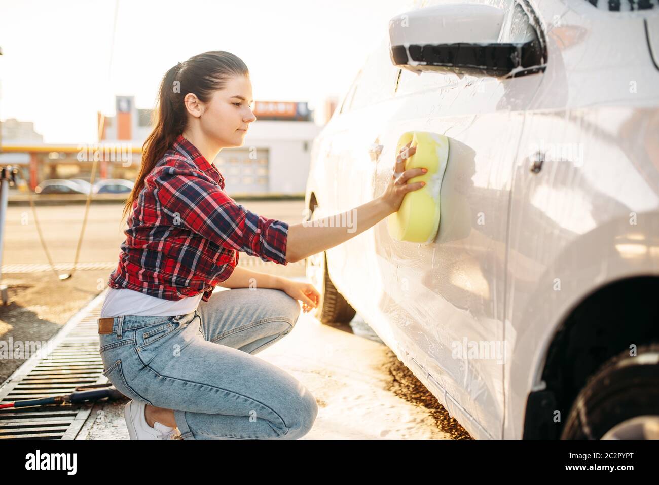 Young woman with sponge scrubbing vehicle with foam, car wash. Lady on ...
