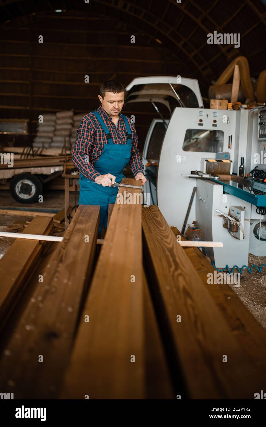 Carpenter in uniform measures the board with caliper, woodworking ...