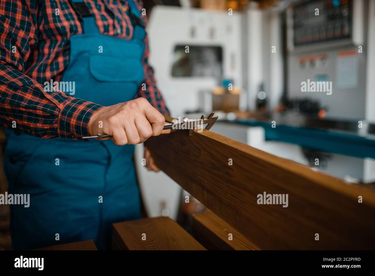 Carpenter in uniform measures the board with caliper, woodworking ...