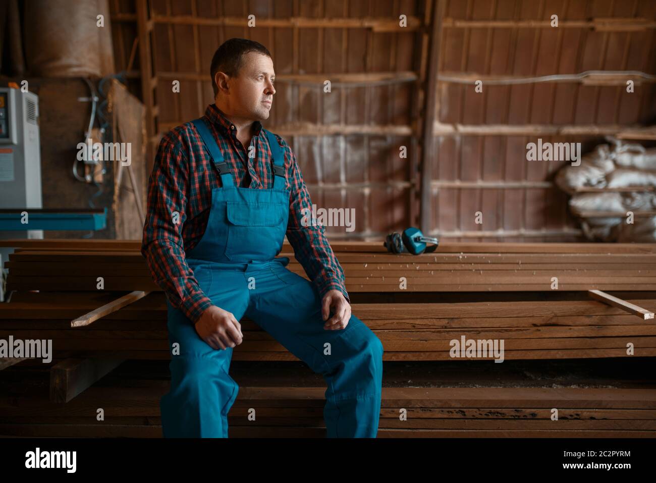 Joiner in uniform at his workplace on timber mill, woodworking machine ...