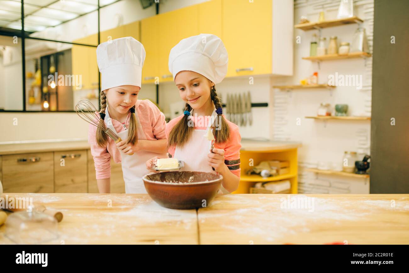Two little girls cooks in caps adds butter to the bowl, cookies ...
