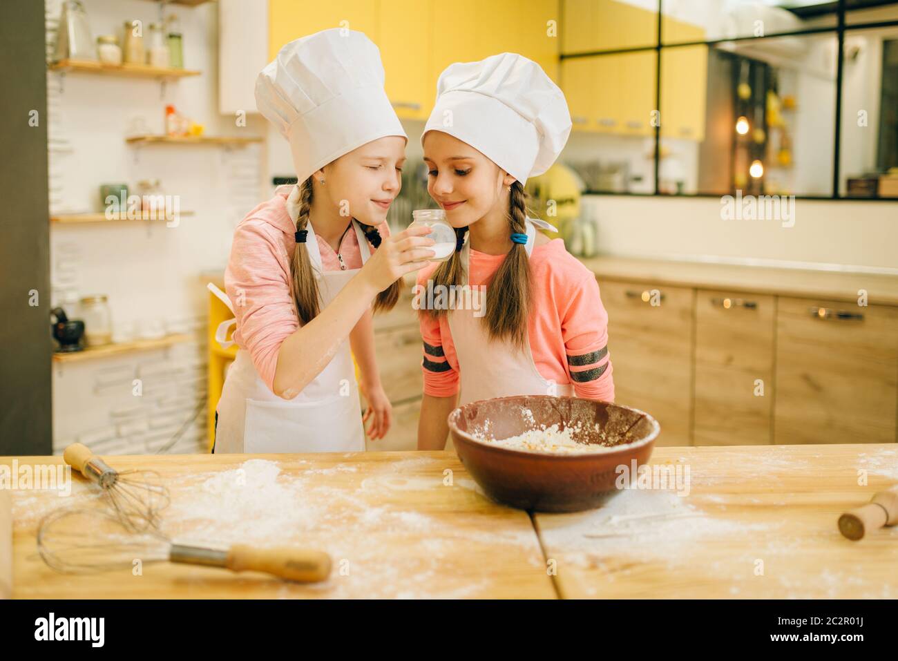 Two little girls cooks in caps sniffing sweet vanilla powder, cookies ...