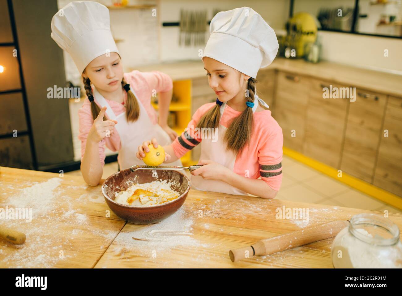 Two little girls cooks in caps rubs lemon to the bowl, cookies ...